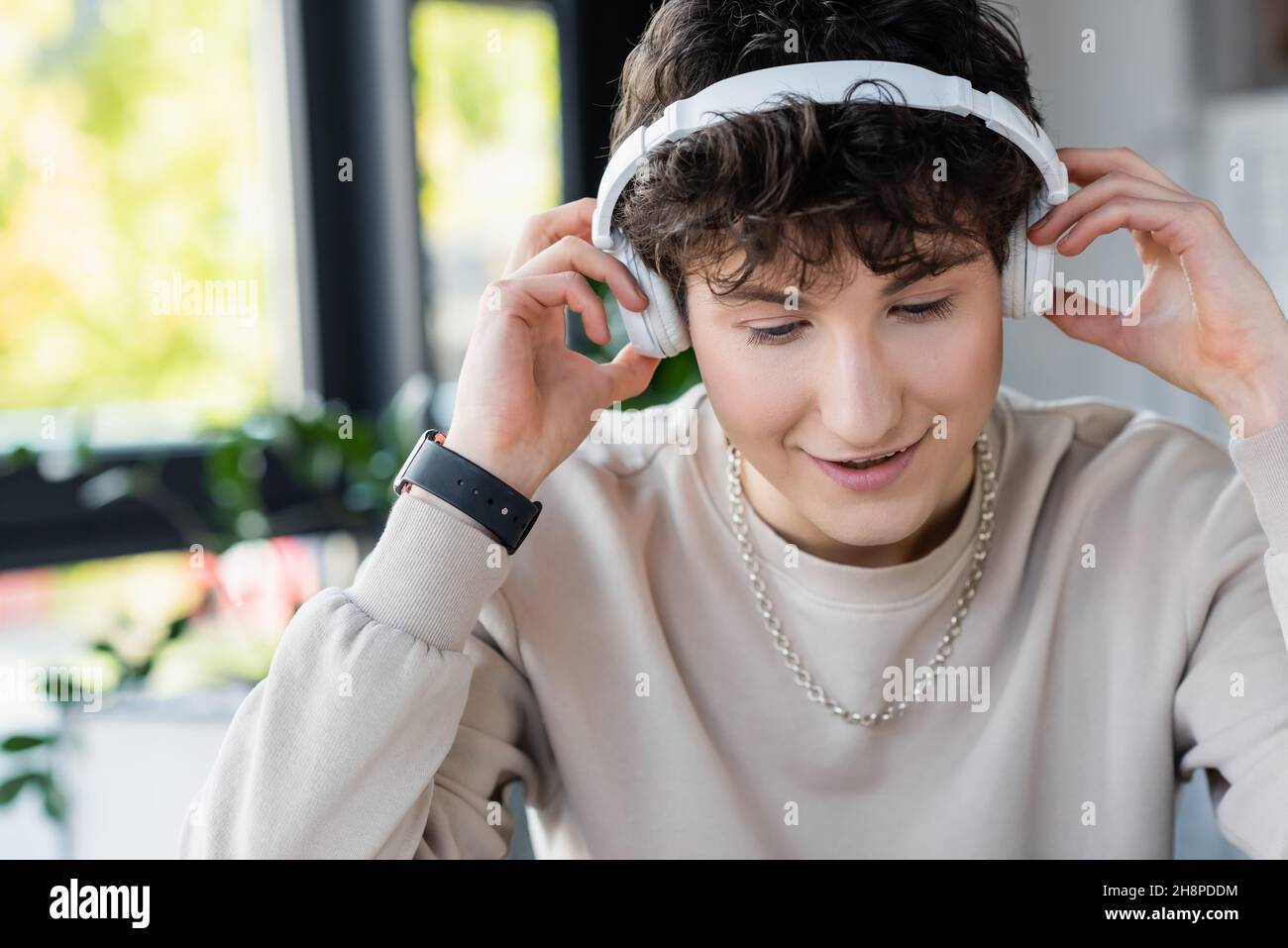 Smiling young transgender person using headphones in office,stock image ...