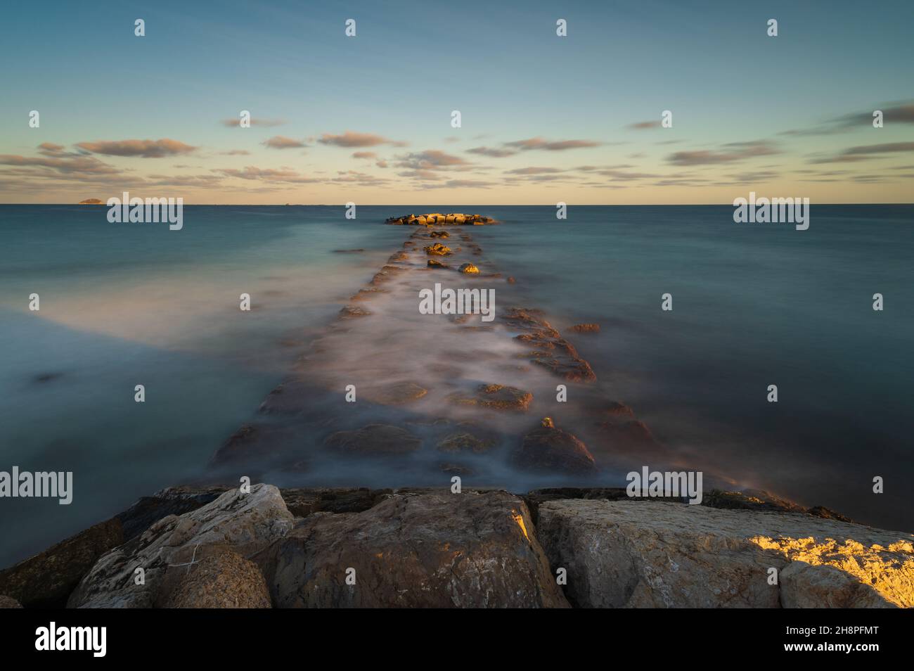 Coastal breakwater overflown with water during high tide at sunset ...