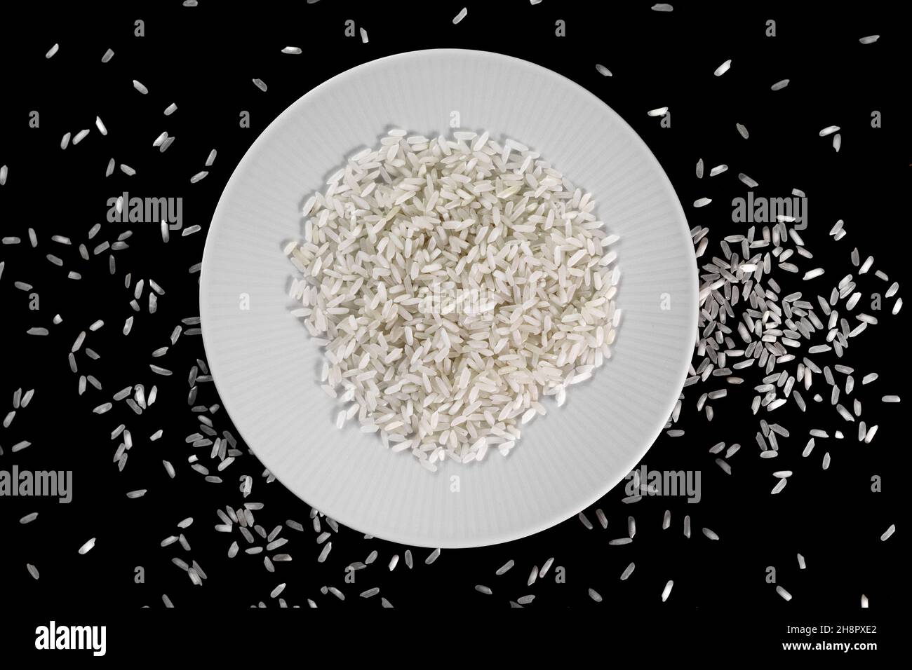Rice in a white plate and grains spilled on a black background Stock ...
