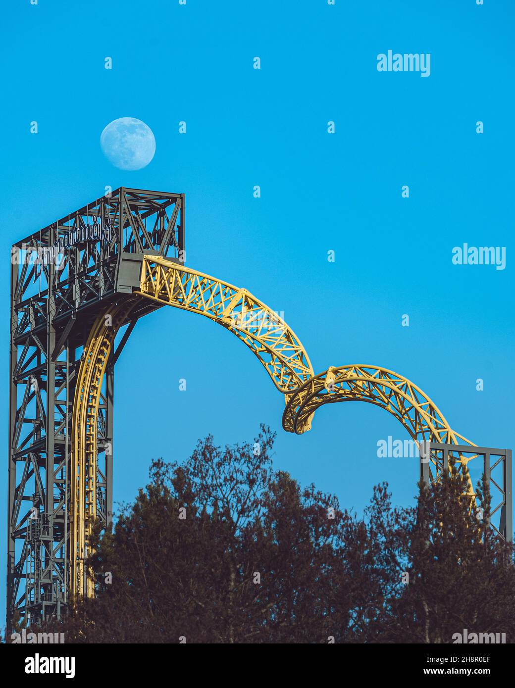 Vertical shot of a rollercoaster in an amusement park under a blue sky ...