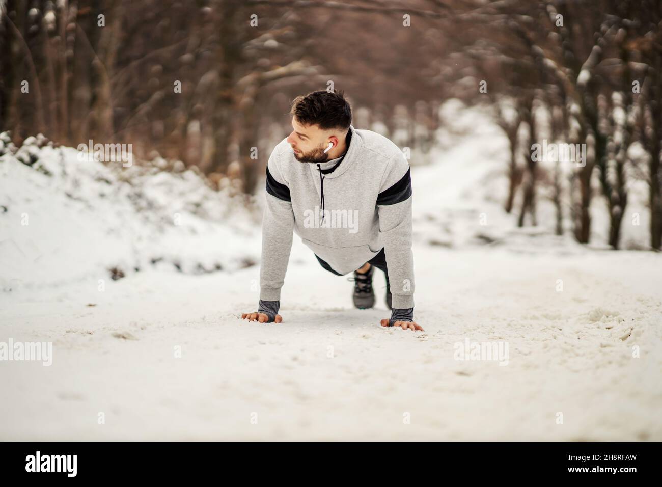 Strong sportsman doing push ups in nature on snowy path at winter ...