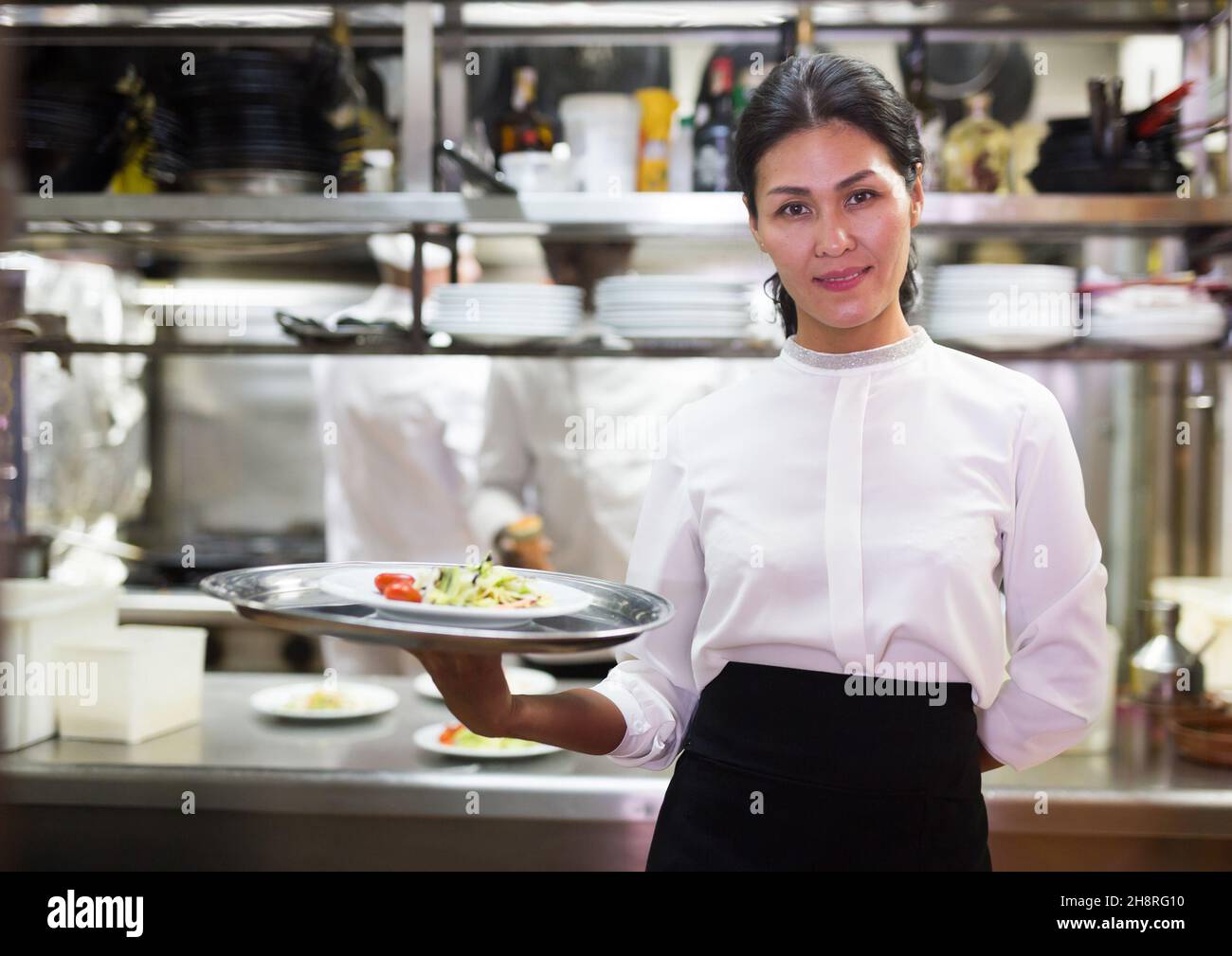 Smiling waitress with ordered dishes in kitchen of restaurant Stock ...