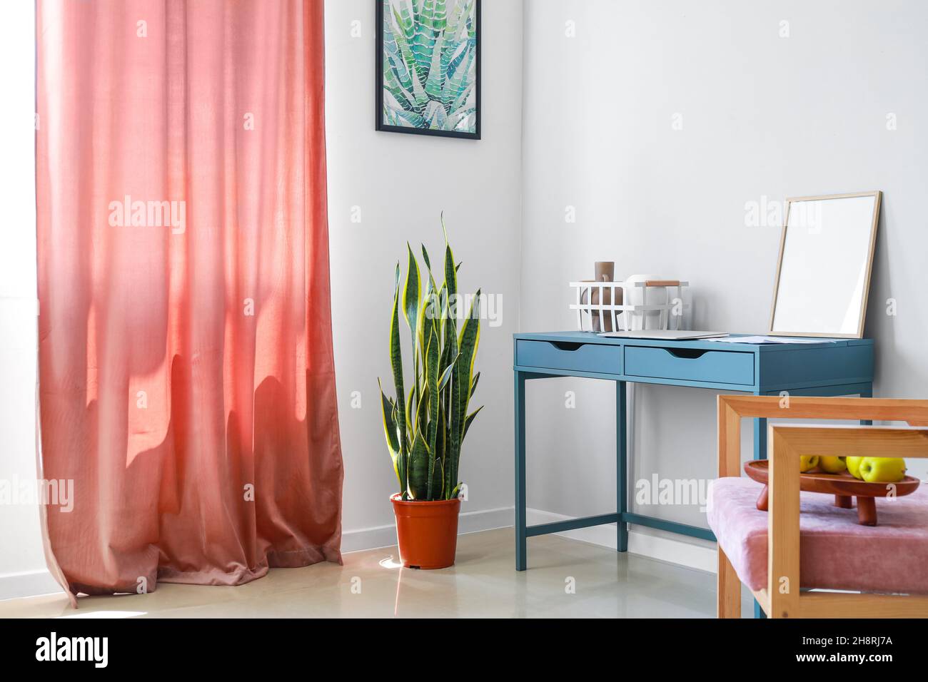 Blue table with blank frame, basket, vases and laptop near light wall ...