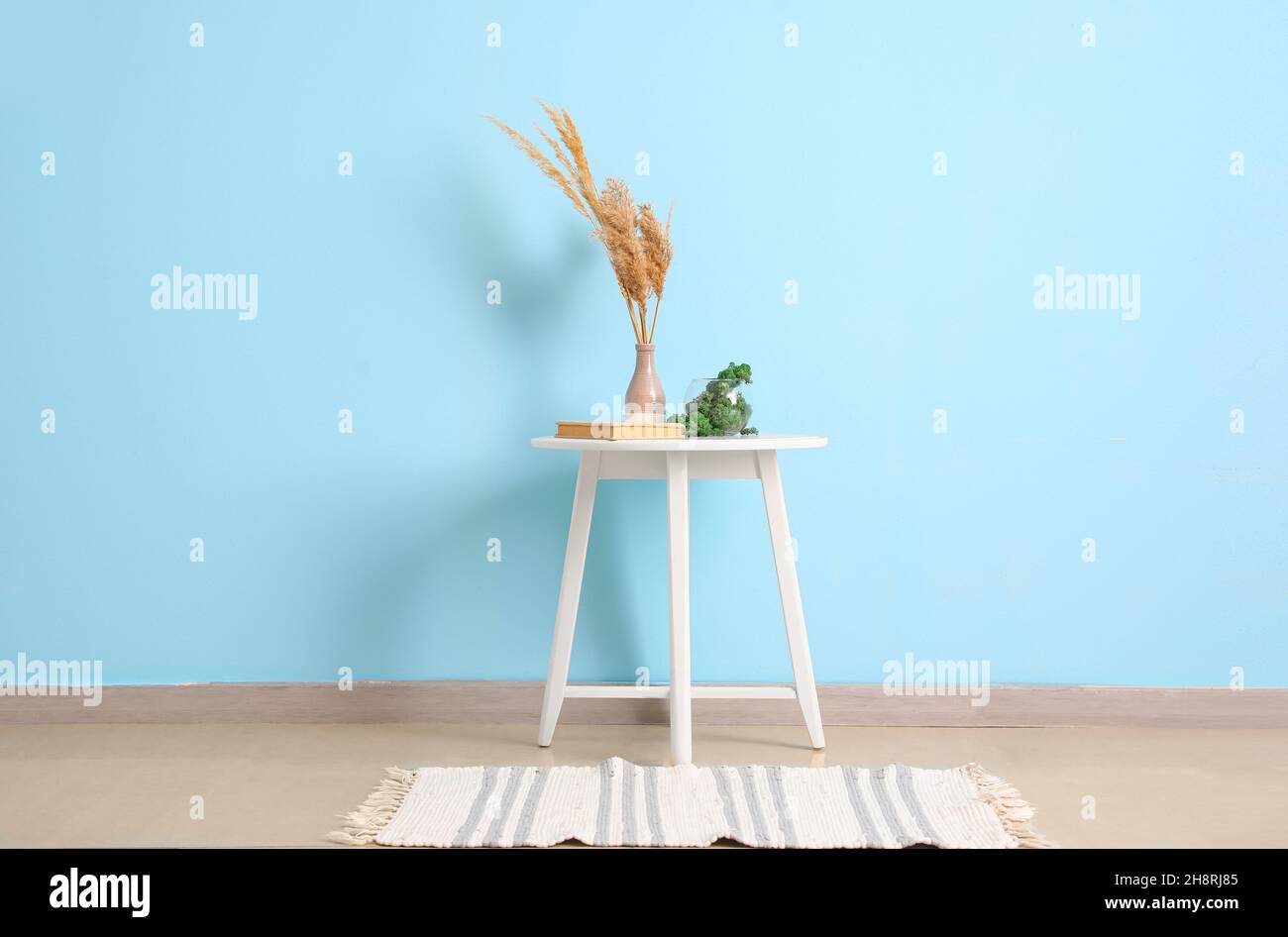 Vase with dry reeds, book and decorative moss on table near blue wall ...