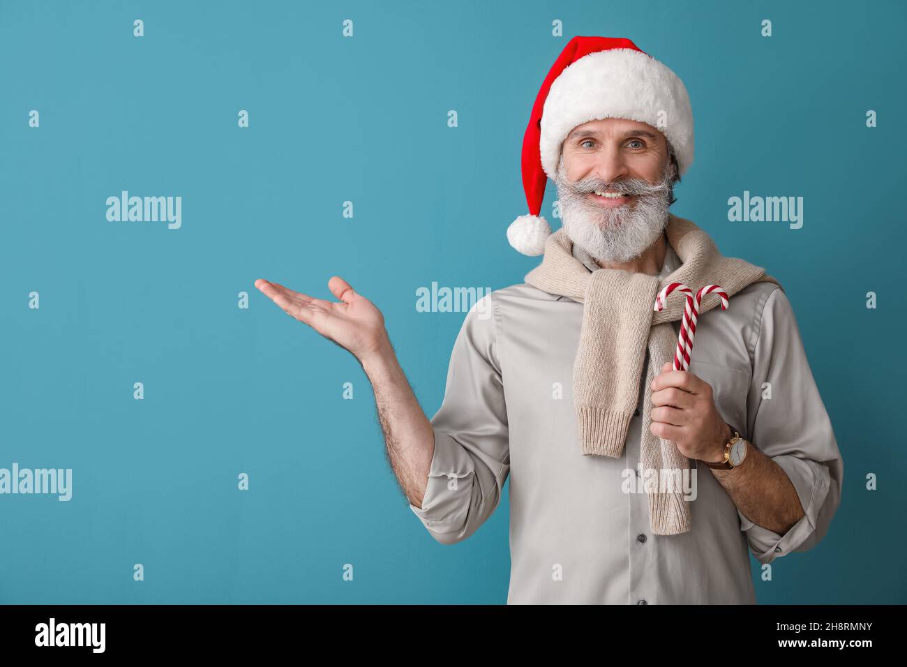 Senior man in Santa hat and with sweet candy canes on color background ...