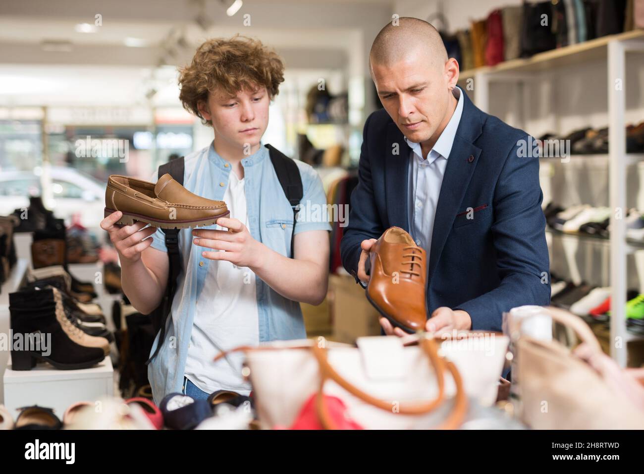 Shoe store employee helping teen to choose classic brown shoes in shoe ...