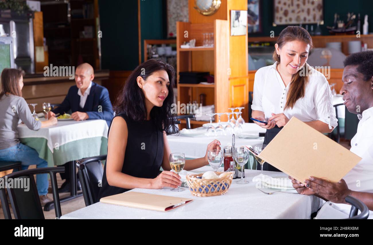 Polite young waitress helping with menu to African American Stock Photo ...
