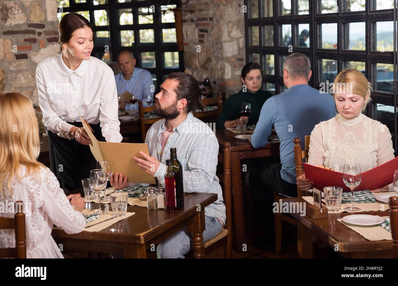 Charming young waiter receiving order from guests in country restaurant ...