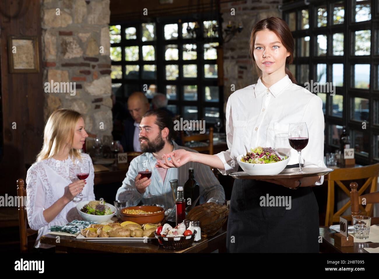 Positive woman waiter demonstrating country restaurant to visitors ...