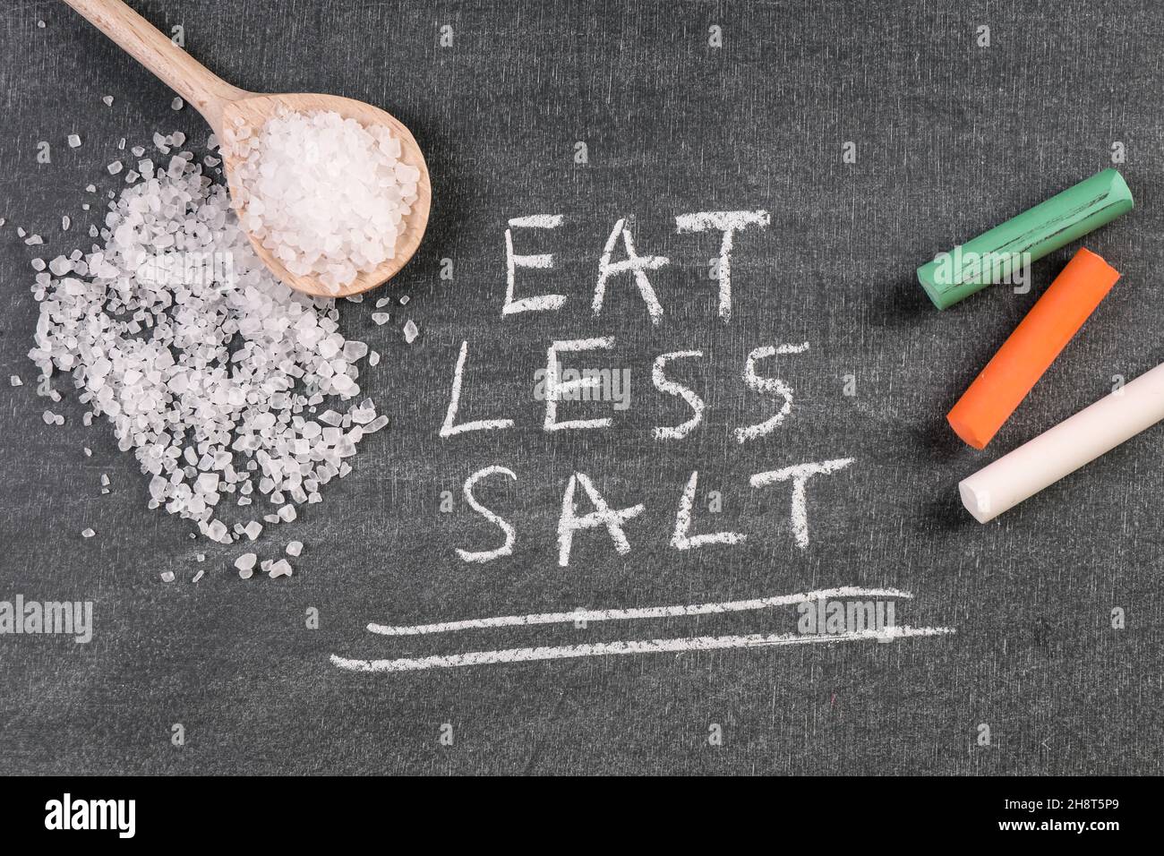 Eat Less Salt. Wooden spoon and chalk pieces on a chalk board Stock ...