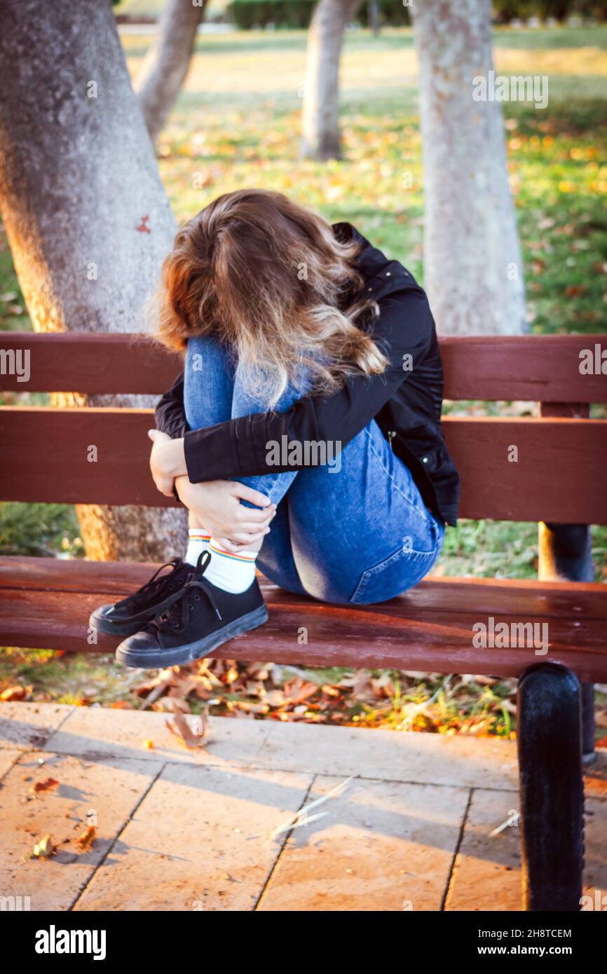 Sad teenager girl sitting on the bench in autumn park. Crying young ...