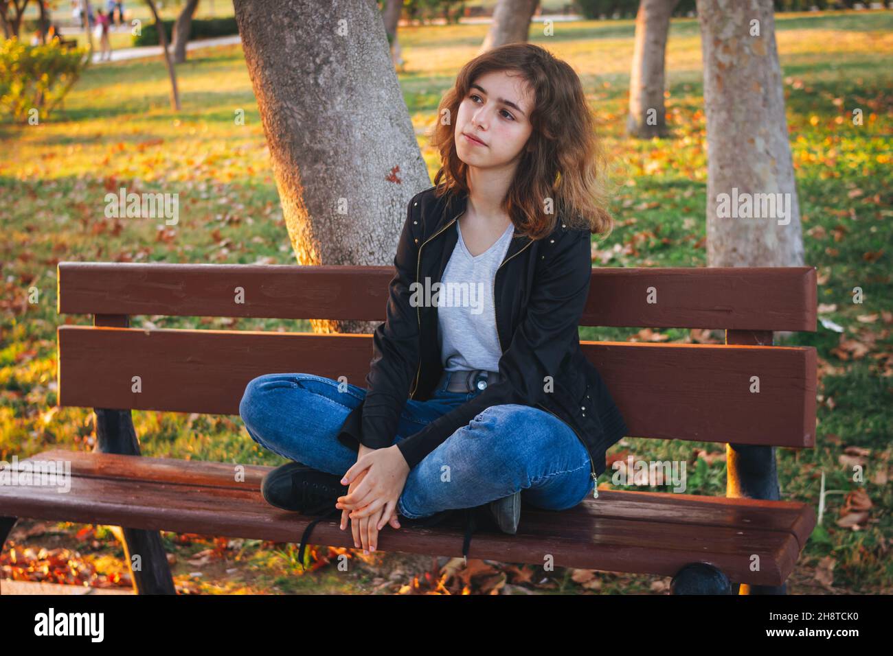 Cheerful teenager girl sitting on bench at autumn park Stock Photo - Alamy