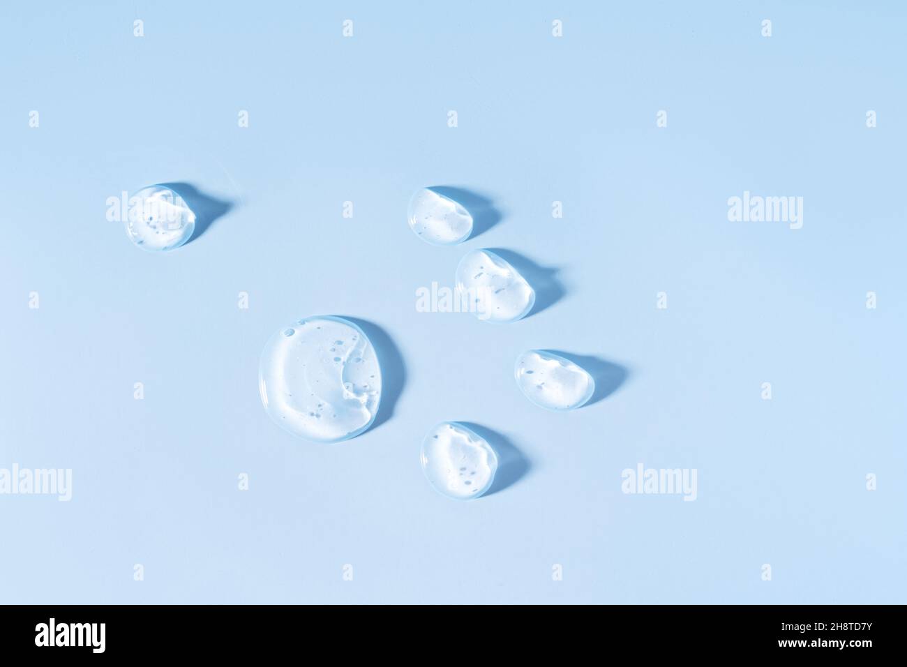 Six drops of clear serum on blue background Stock Photo - Alamy