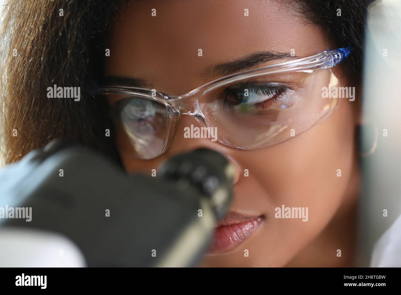 A dark-skinned woman looks through a microscope Stock Photo - Alamy