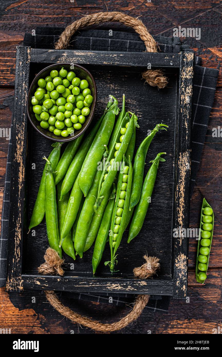 Raw green pea pods in a wooden tray. Dark wooden background. Top view ...