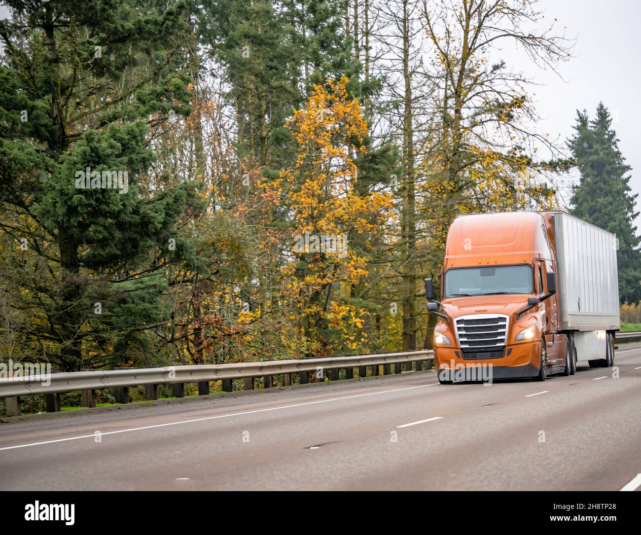 Industrial big rig orange semi truck tractor with turned on headlight ...