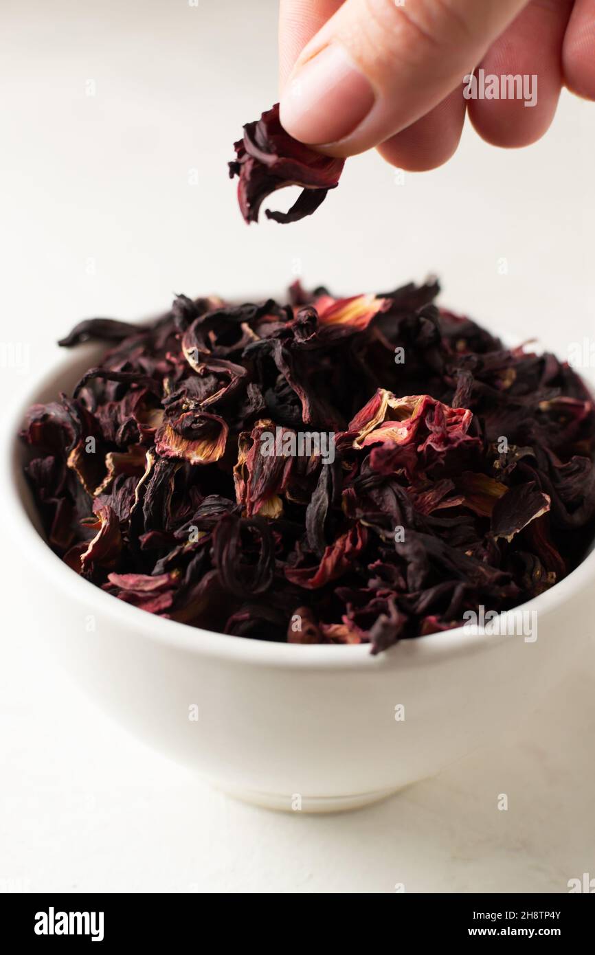 Dry leaves of hibiscus lie in a white bowl, a woman's hand raises one ...