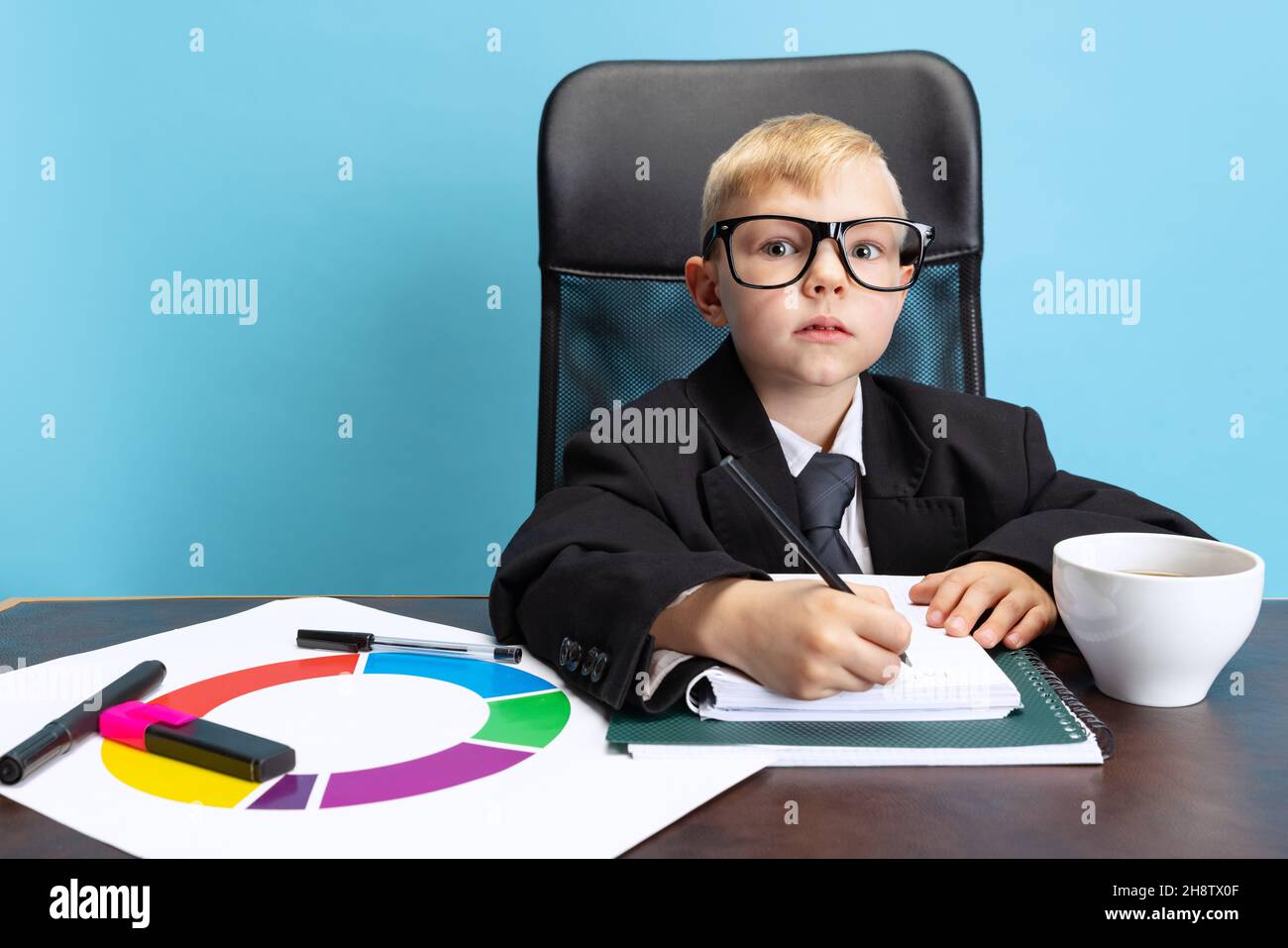 Portrait of little boy, child businessman in huge jacket suit sitting ...