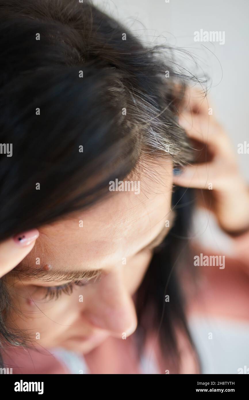 Portrait of a beautiful young woman examining her scalp and hair in ...
