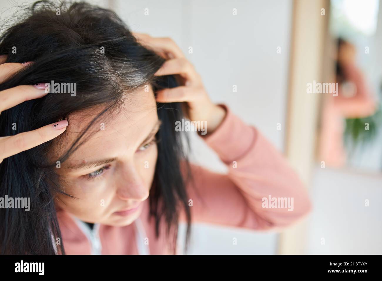 Portrait of a beautiful young woman examining her scalp and hair in ...