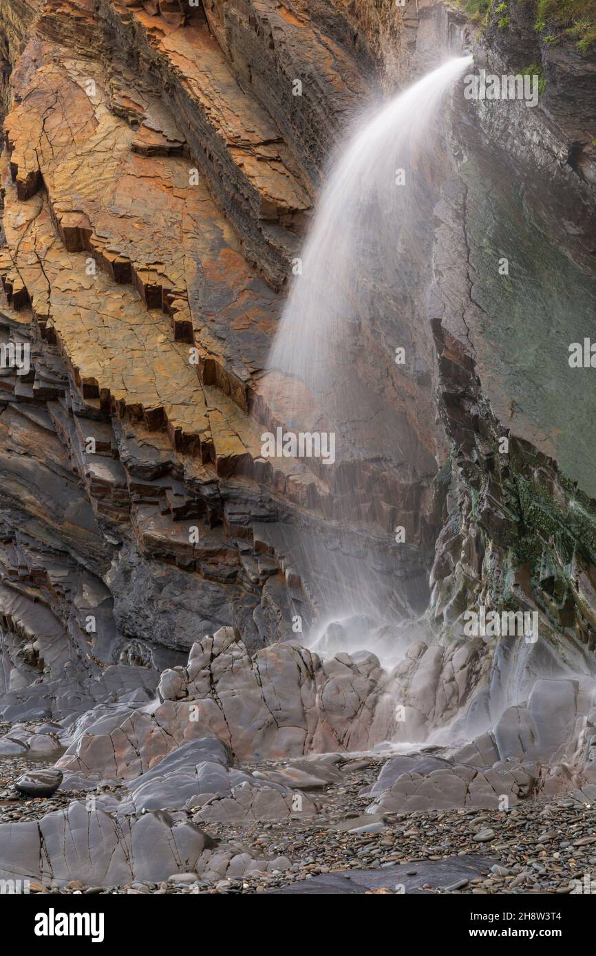 Waterfall against sandstone rock strata on beach at Sandymouth, near ...