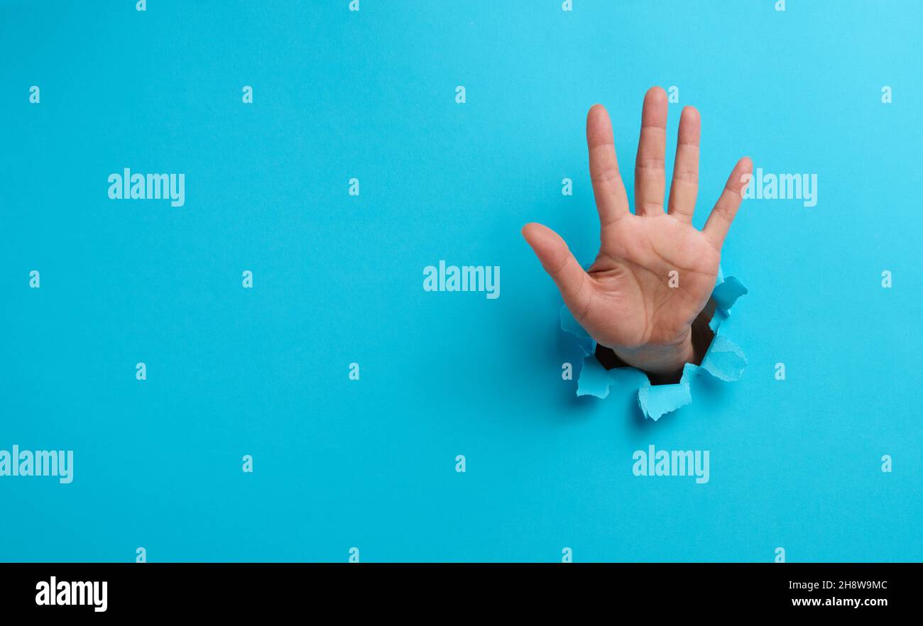 a woman's hand with an open palm sticks out of a torn hole in blue ...