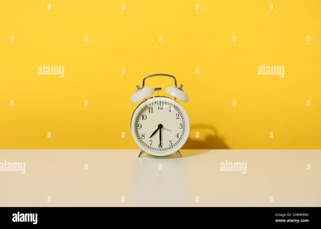 a round alarm clock stands on a white table, half past seven in the ...