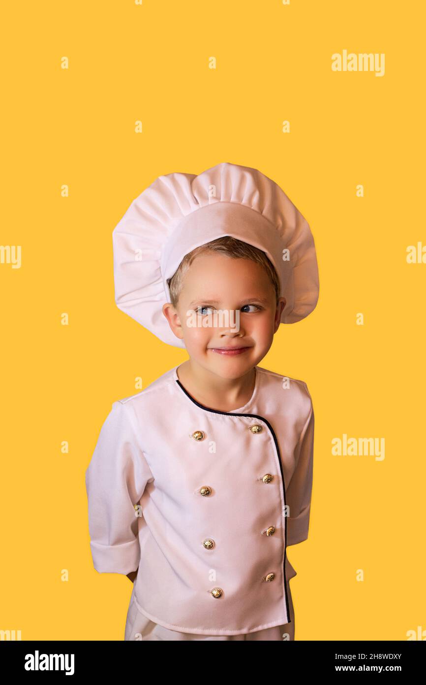 Smiling child in white chef uniform with a funny hat. Cheerful yellow ...