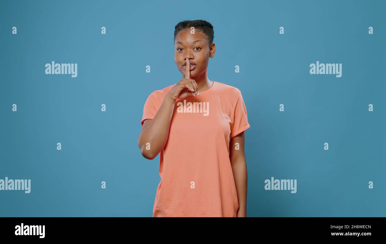 Portrait of woman doing shush gesture with finger on mouth, having ...