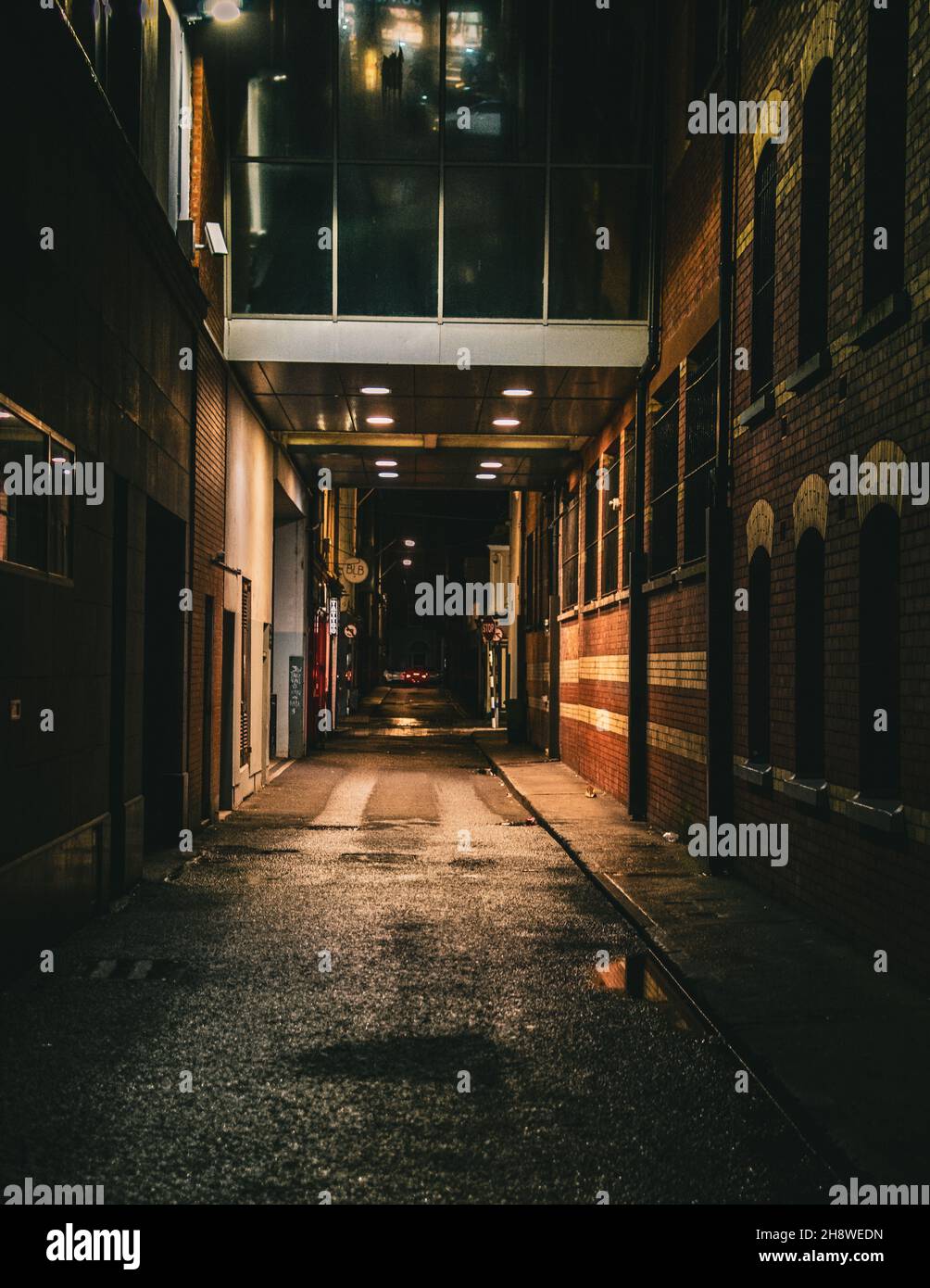 Vertical shot of a dark alley at night with a footbridge above it ...