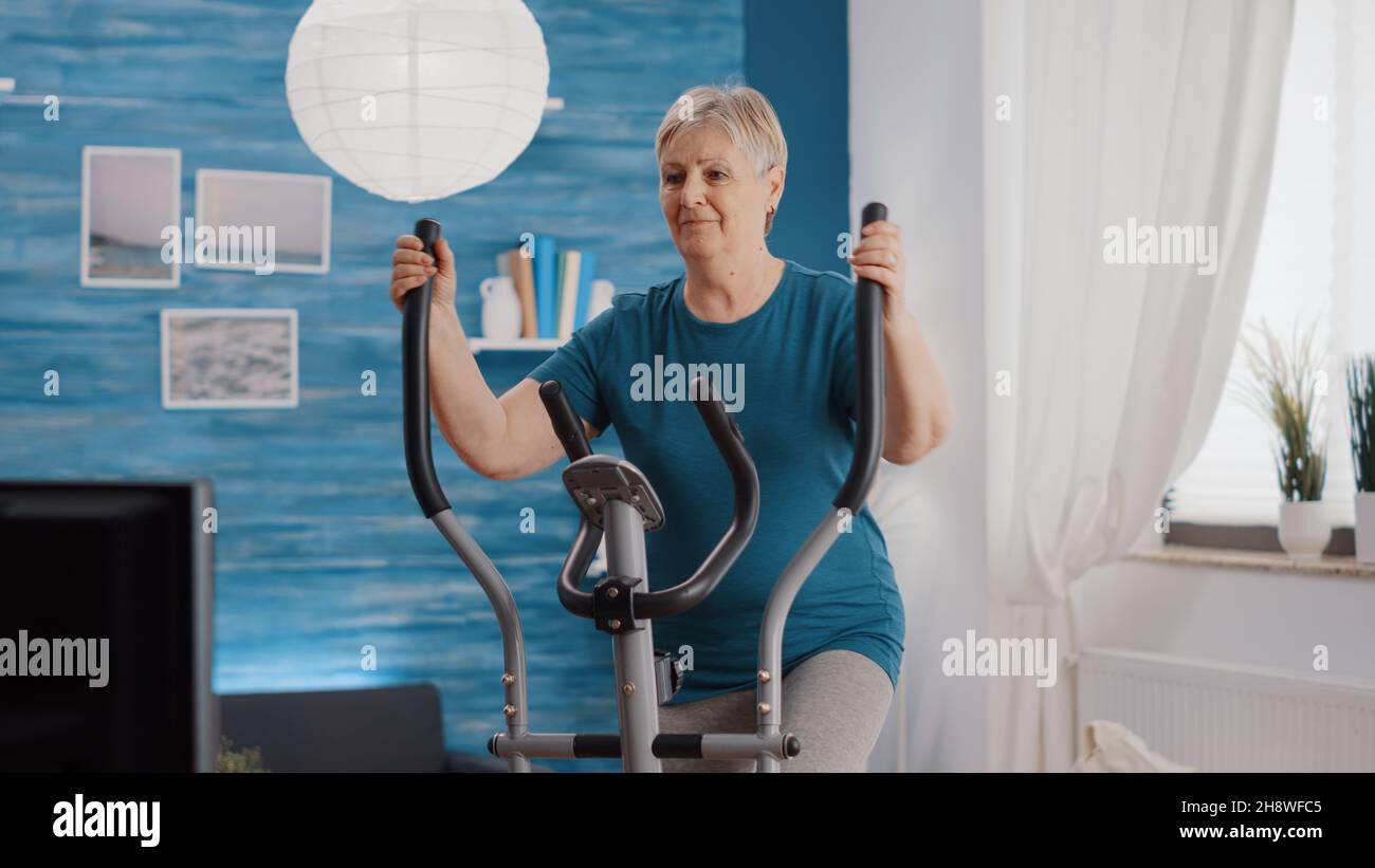 Retired woman training with stationary bicycle at home. Senior adult ...