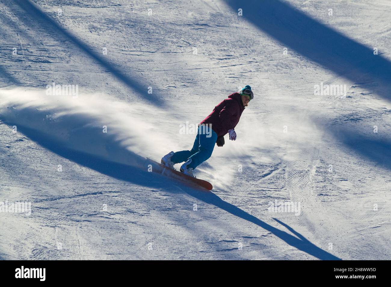 A girl on a snowboard slides down a ski slope. On a curve, a plume of ...