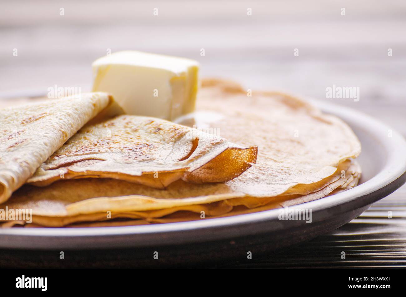 Stack of French crepes with butter in ceramic dish on wooden kitchen ...