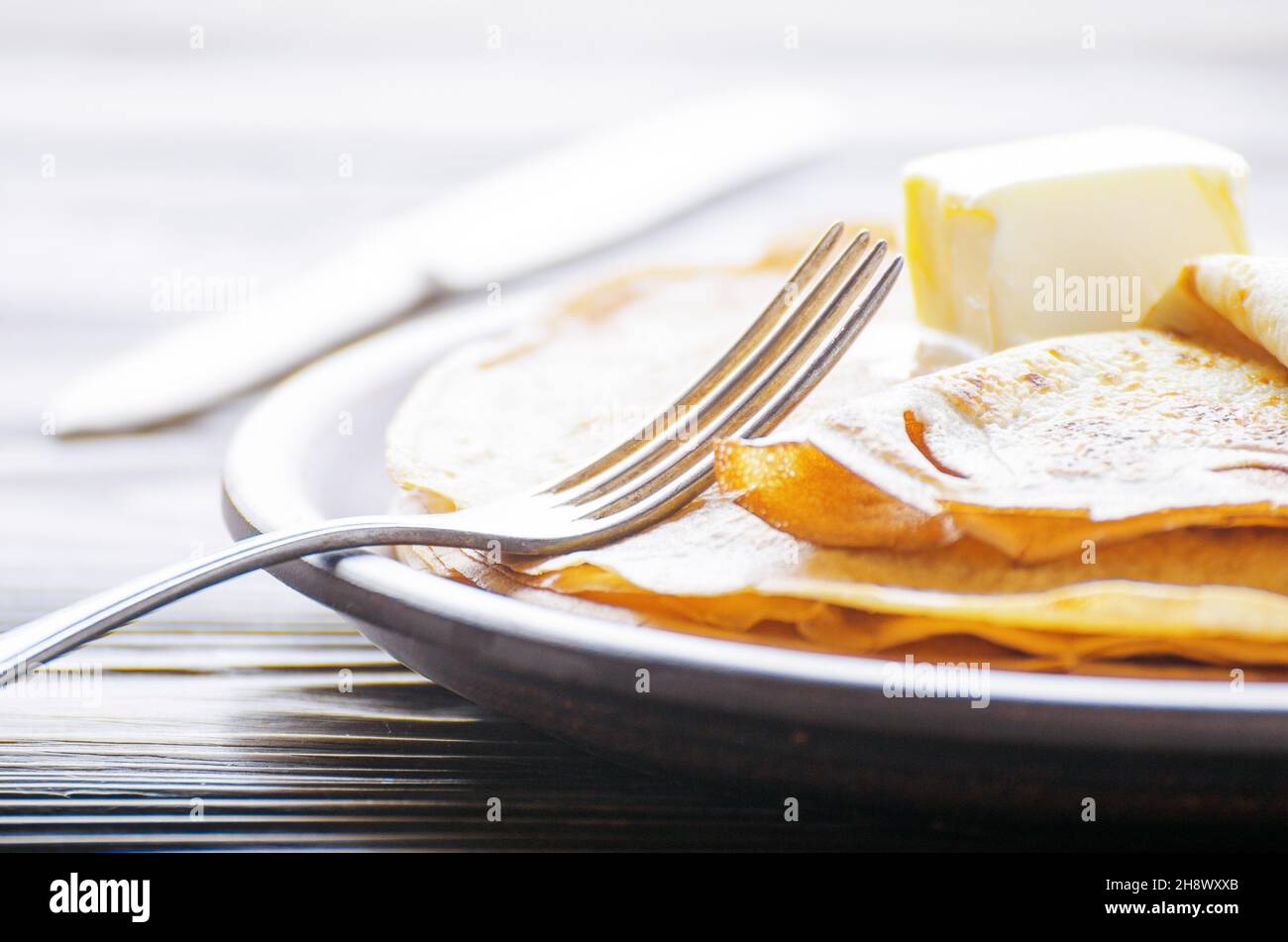 Stack of French crepes with butter in ceramic dish on wooden kitchen ...