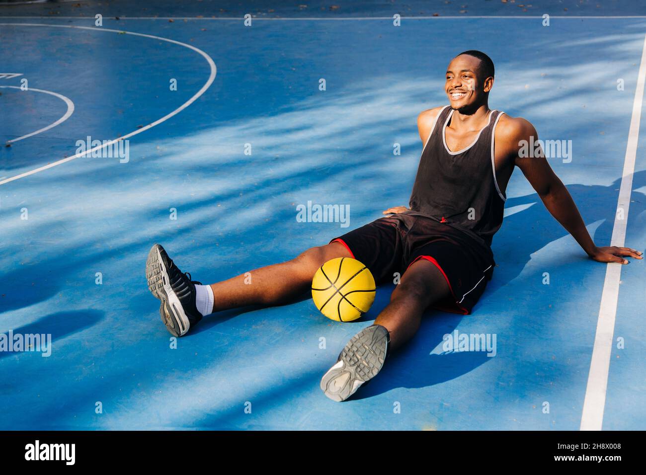 Full body of young African American athlete in sportswear sitting on ...