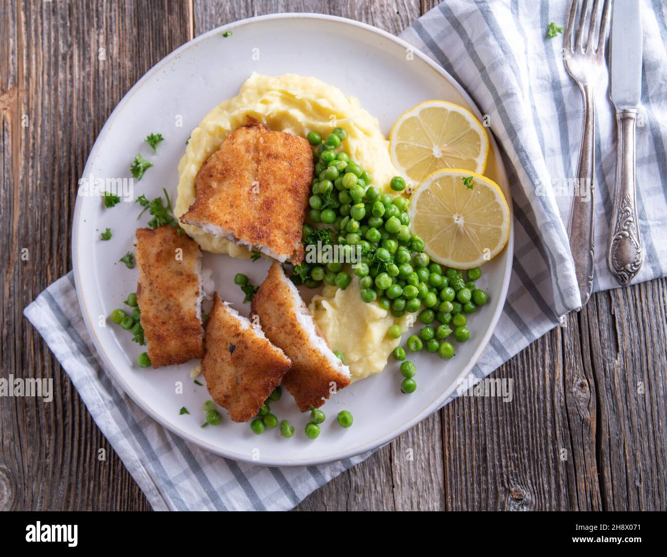 Breaded fish with mashed potatoes and green peas on a plate on wooden ...