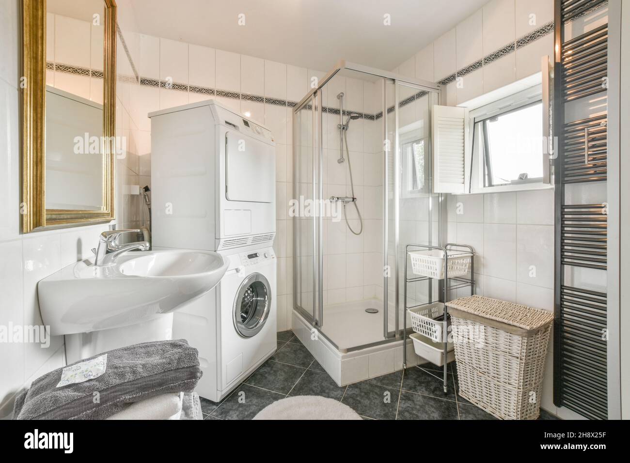 Modern white washing machine with dryer placed near glass shower cabin ...