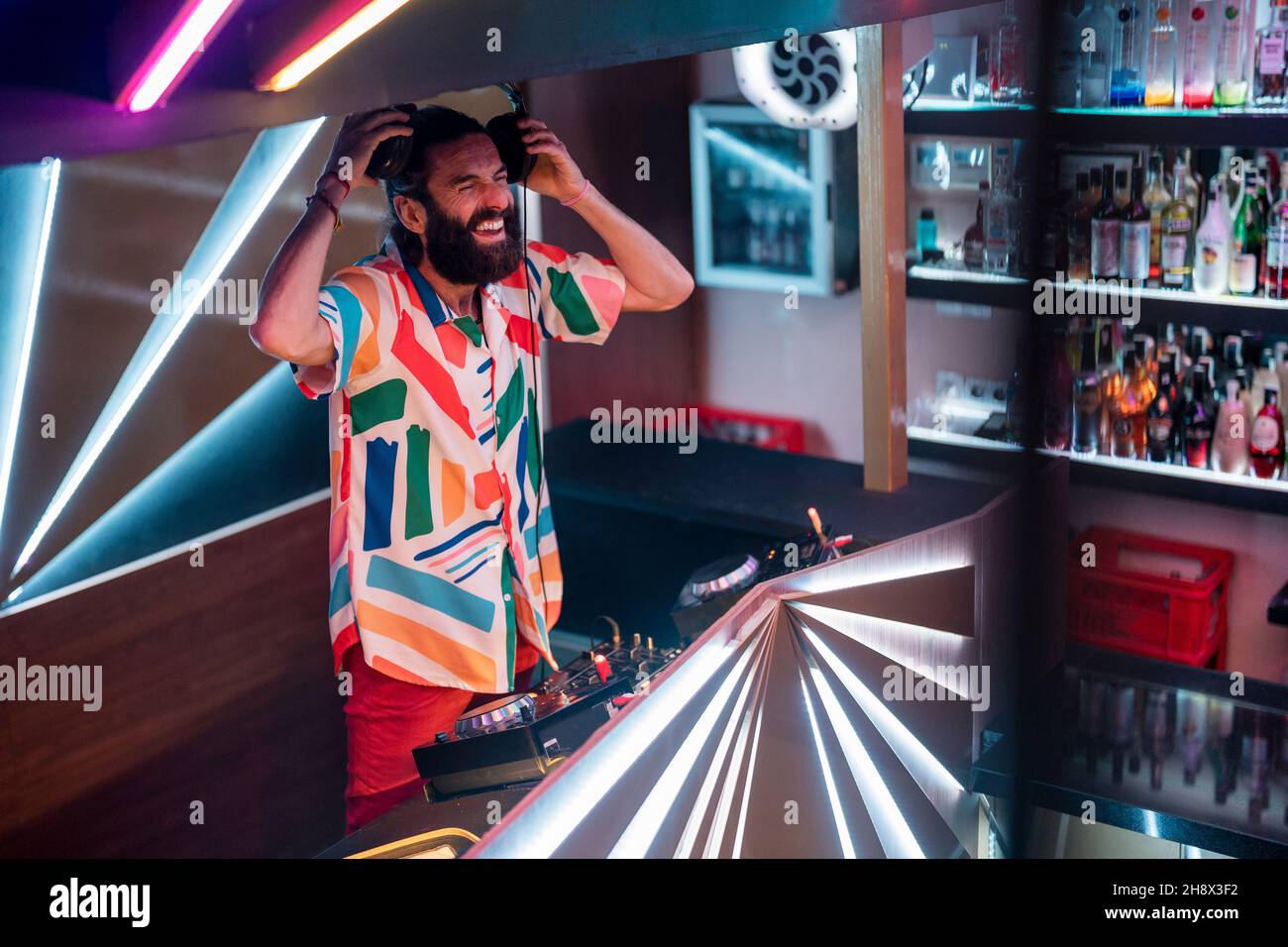 Cheerful young bearded male DJ in colorful shirt and headphones ...