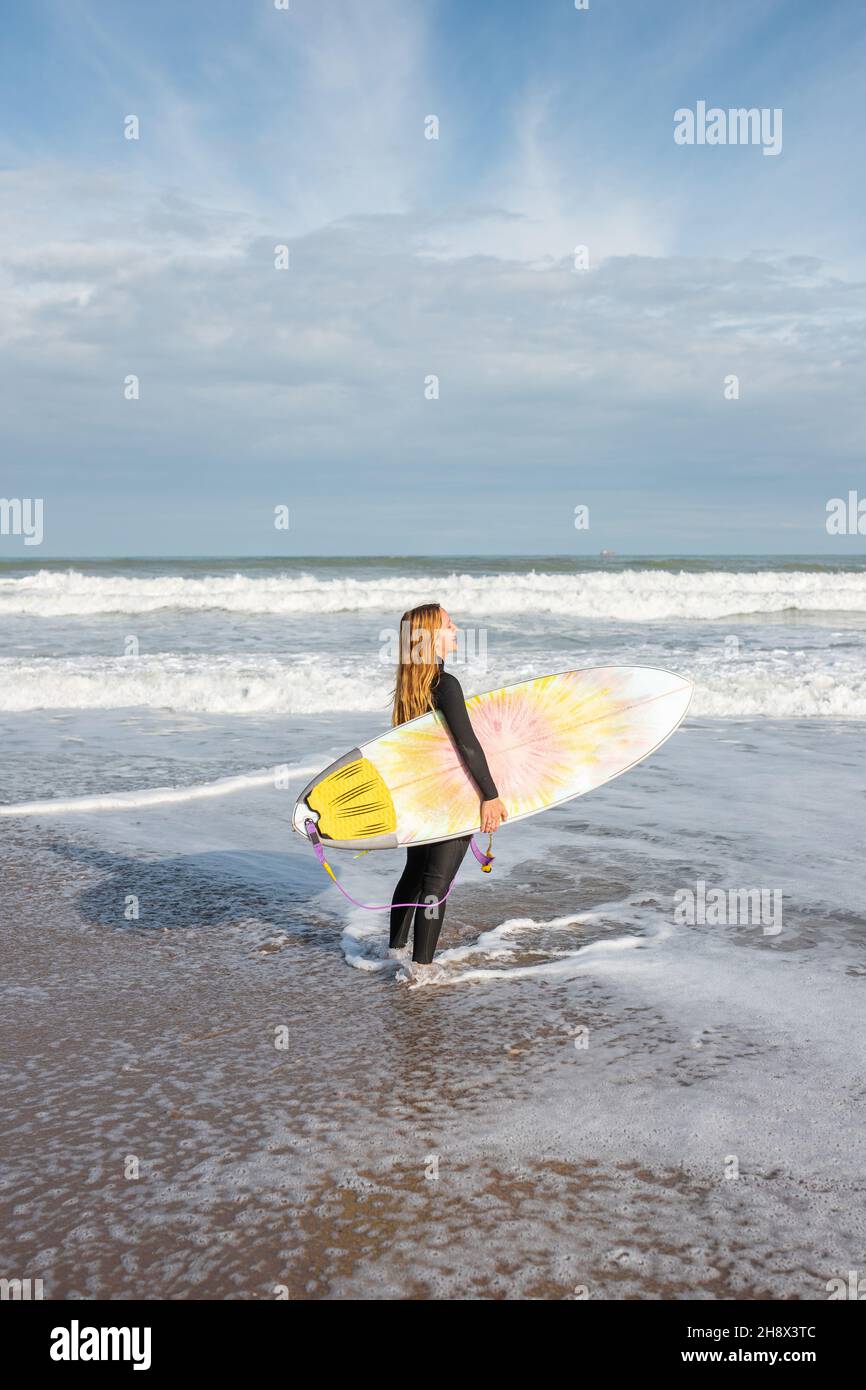 Full body side view of sportive female surfer in black wetsuit walking ...