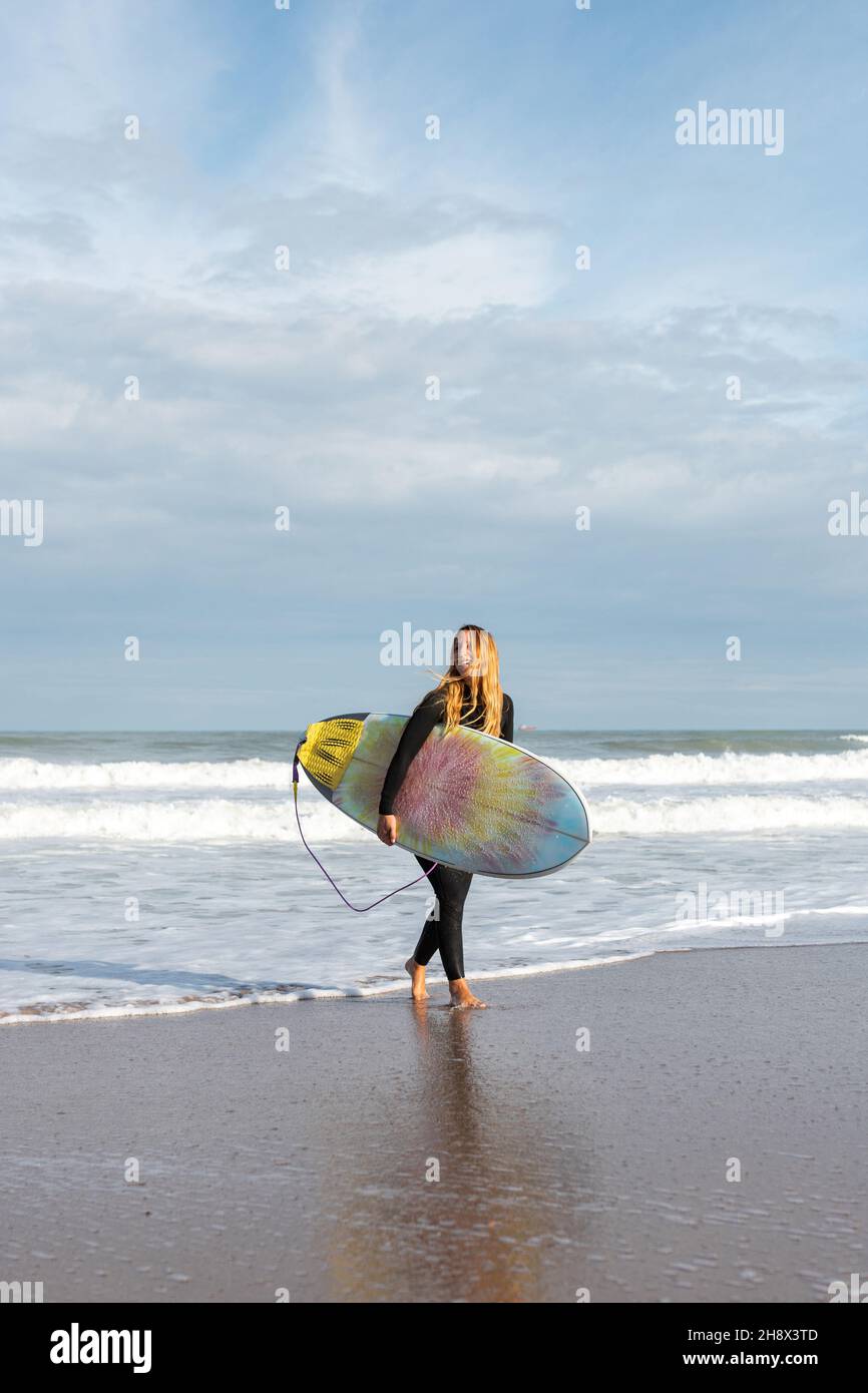 Full body side view of sportive female surfer in black wetsuit walking ...