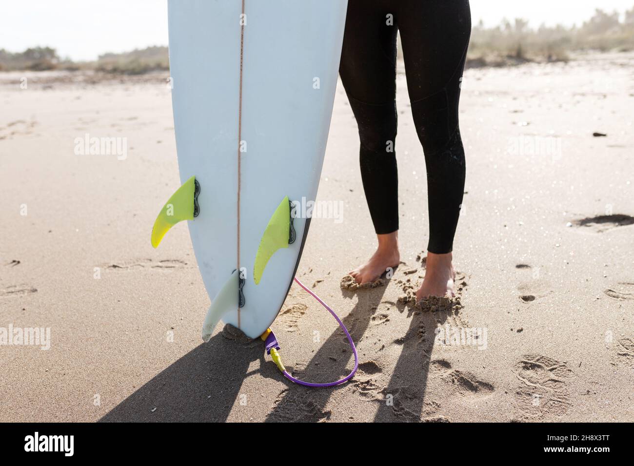 Crop anonymous barefoot surfer with white surfboard with fins standing ...