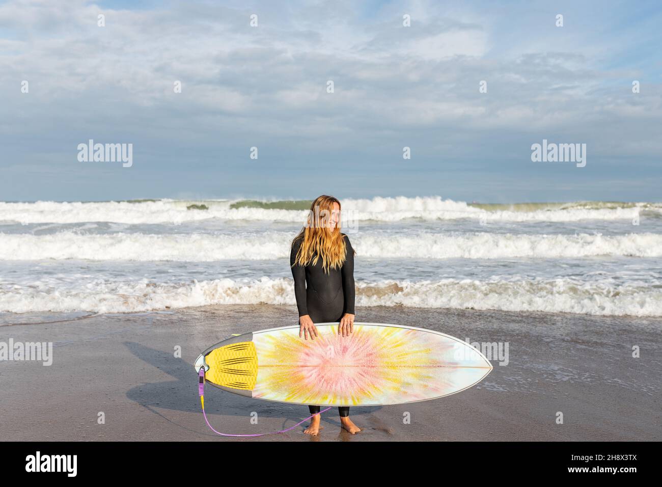 Full body of sportive female surfer in black wetsuit standing on wet ...