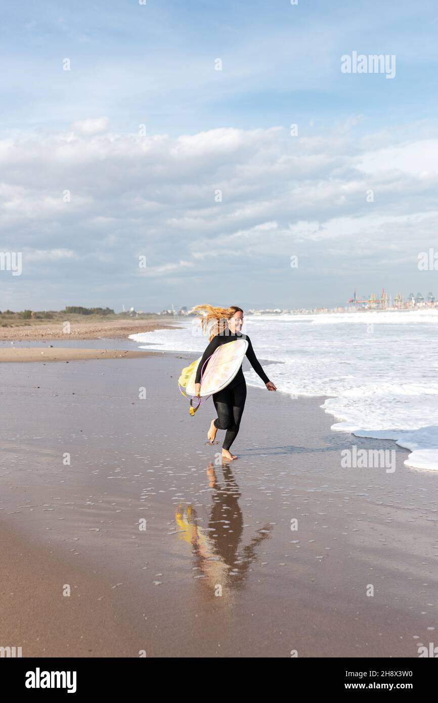 Full body of sportive female surfer in black wetsuit running on wet ...