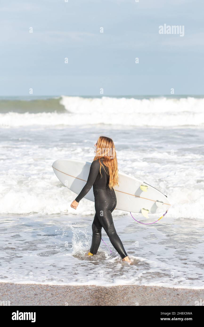 Full body side view of sportive female surfer in black wetsuit walking ...