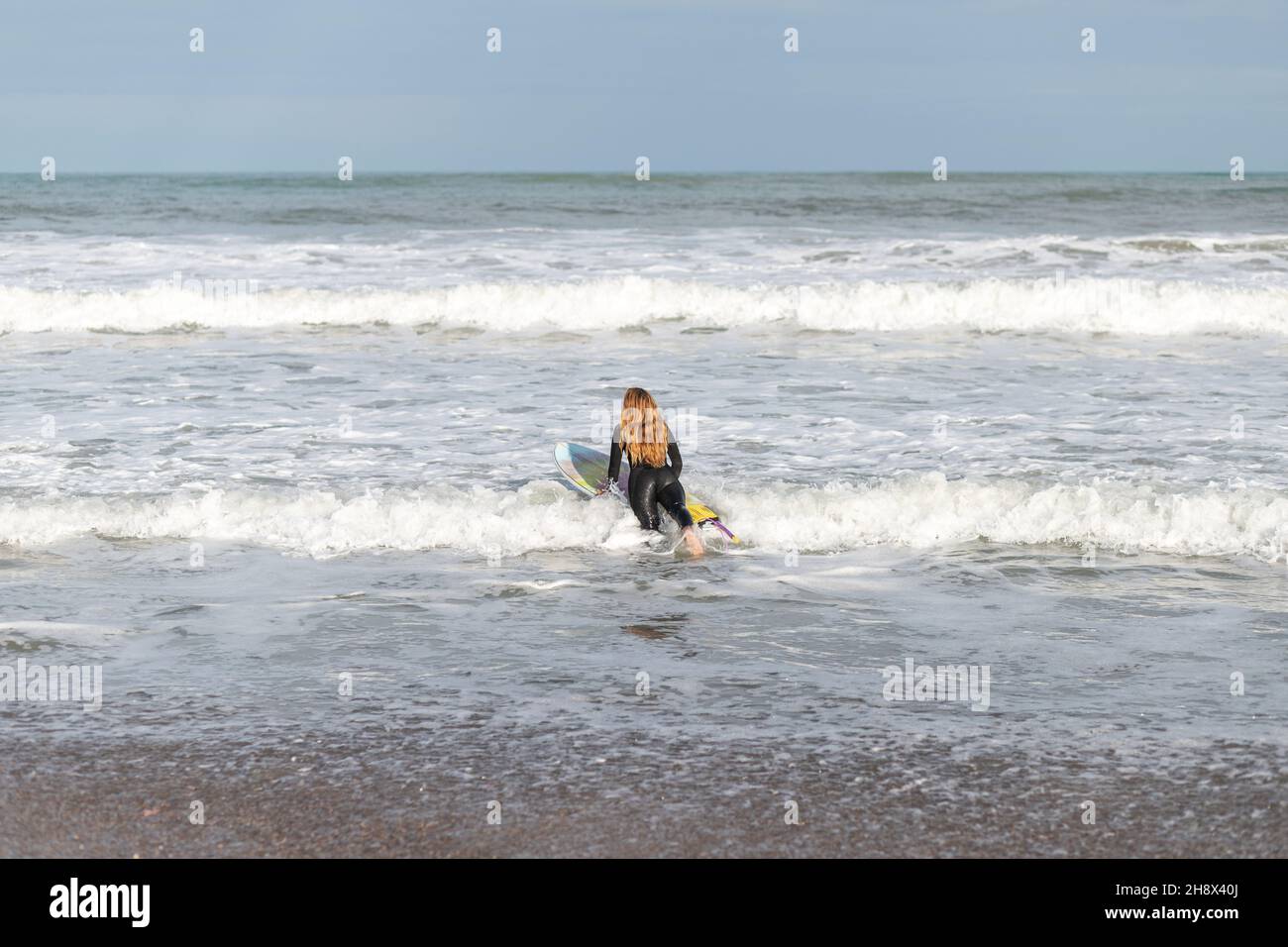 Back view of anonymous Woman surfer in wetsuit with surfboard in waving ...