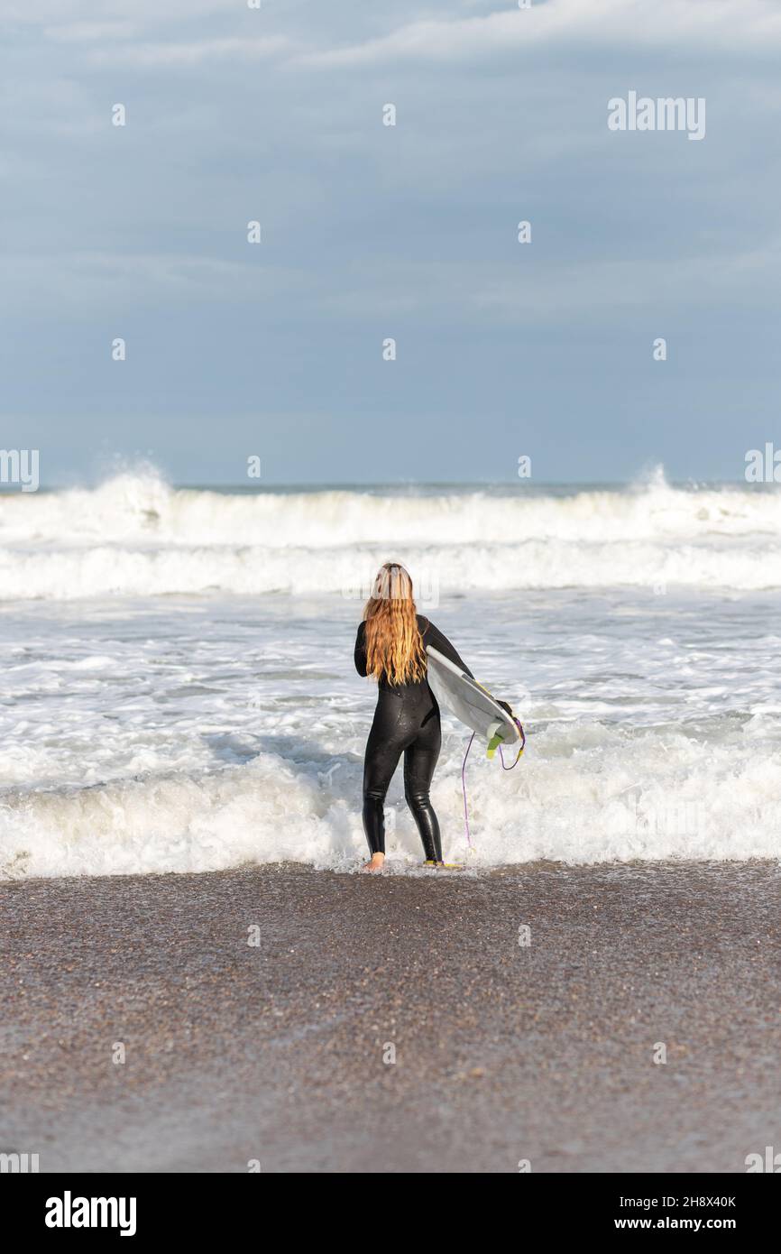 Back view of anonymous Woman surfer in wetsuit standing with surfboard ...