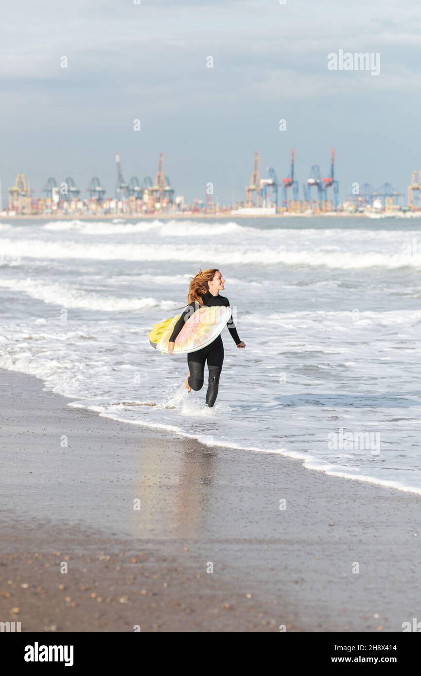 Full body of sportive female surfer in black wetsuit running on wet ...