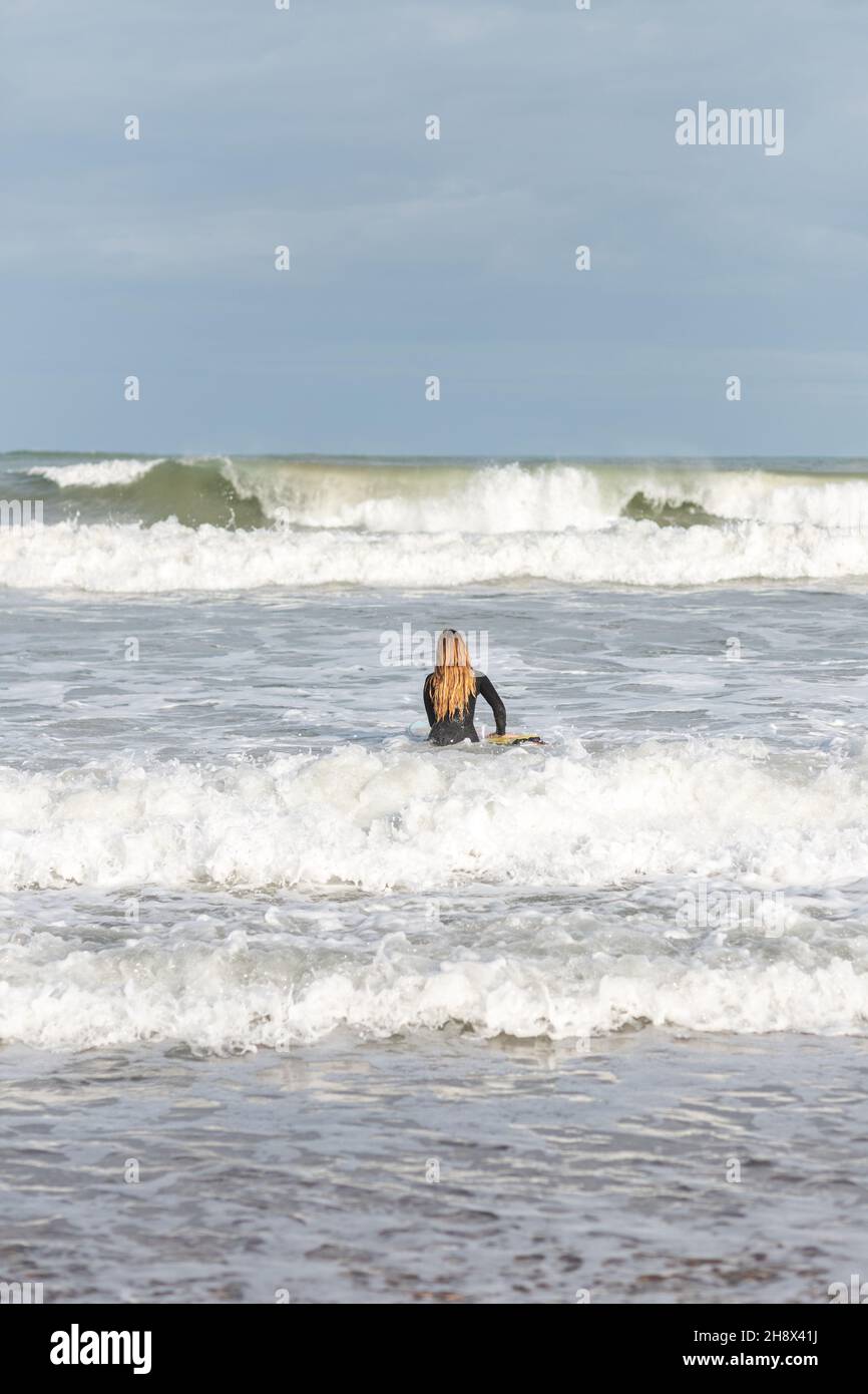 Back view of anonymous Woman surfer in wetsuit with surfboard in waving ...