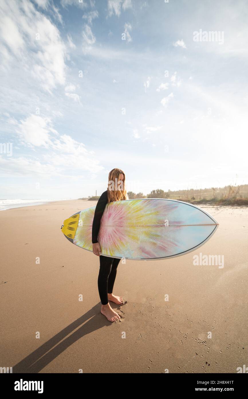 Full body of sportive female surfer in black wetsuit standing on wet ...