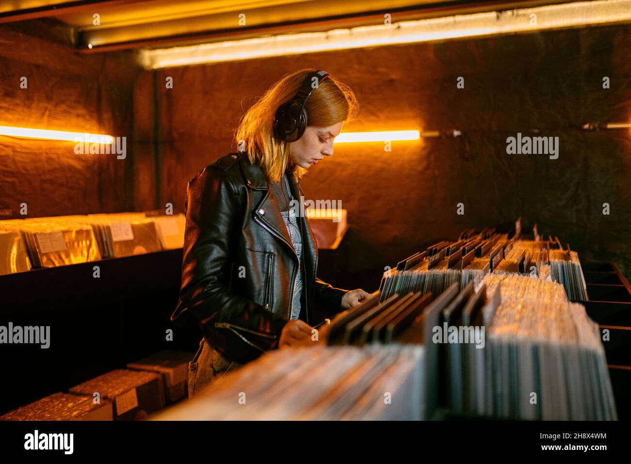 Side view of young female with headphones choosing vinyl record while ...